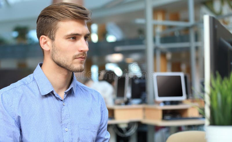 Young Man Sitting and Looking at Computer Monitor while Working in ...