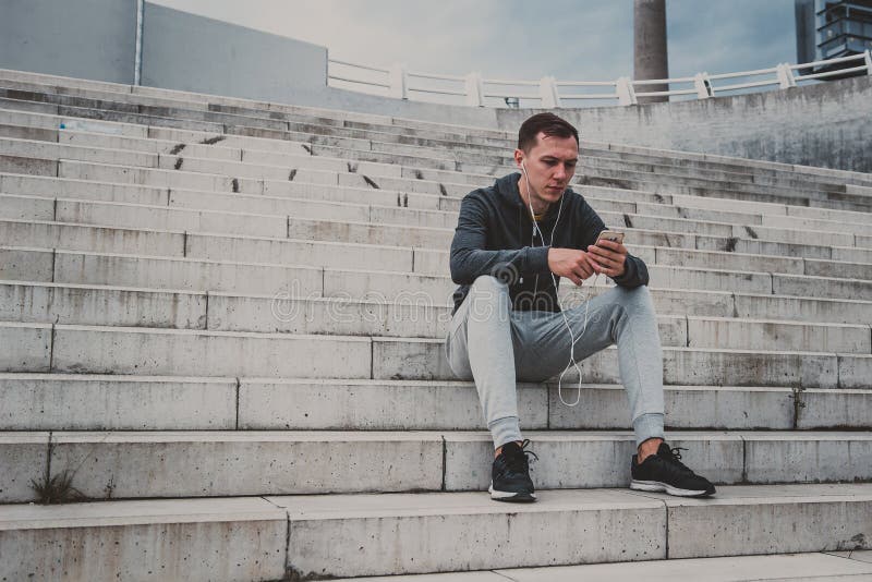 Young Man Sitting on the Modern Bridge in the City, Using His ...