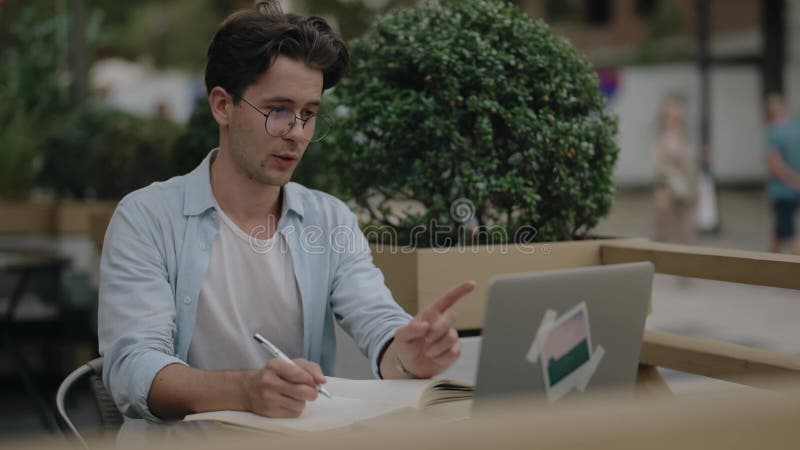 Young Man Working on Laptop and Taking Notes at Outdoor Cafe Stock ...