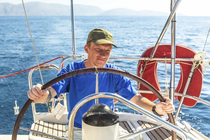 Young Man Skipper at the Helm Controls Sailing Yacht. Sport. Stock ...