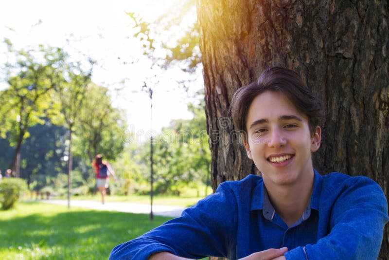 Young Man Smiling and Sitting at Grass beside Tree at Park. Stock Photo ...