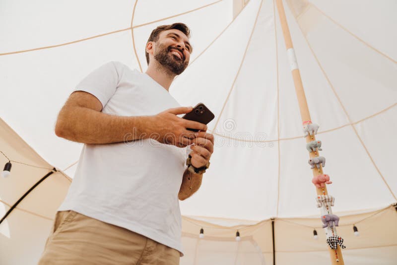 Young Man Smiling and Using Cellphone while Resting in Big Tent Stock ...