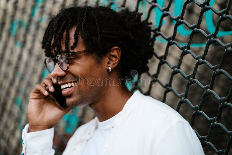 Young Man Smiling and Using Cellphone Standing Over Chain Link Fence ...