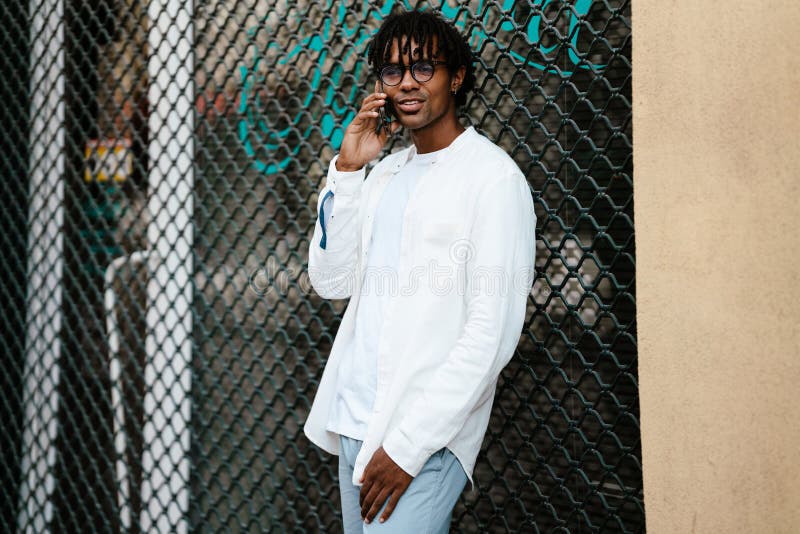 Young Man Smiling and Using Cellphone Standing Over Chain Link Fence ...