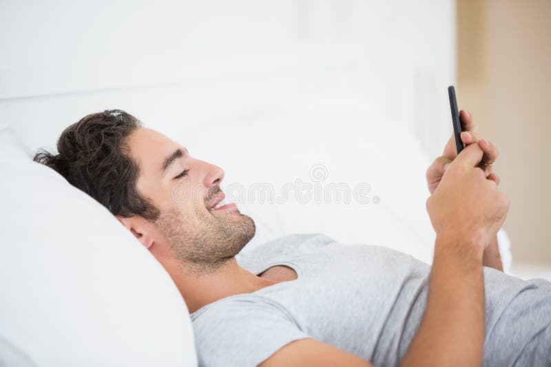 Young Man Smiling while Using Mobile Phone on Bed Stock Image - Image ...