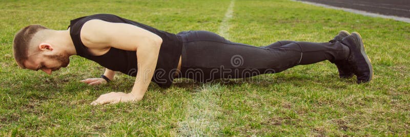 Young Man in Sportswear Does Exercises on the Grass at the Stadium ...