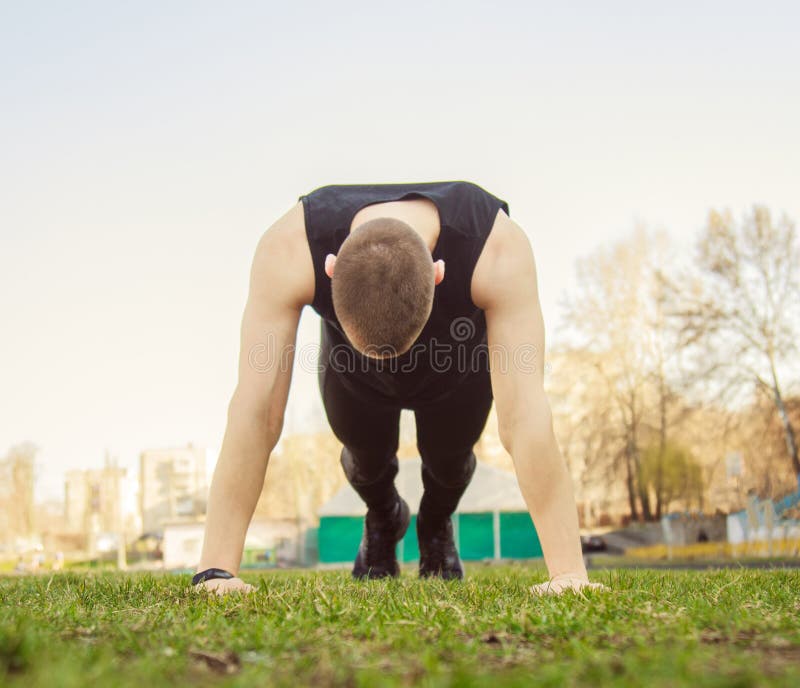 Young Man in Sportswear Does Exercises on the Grass at the Stadium ...