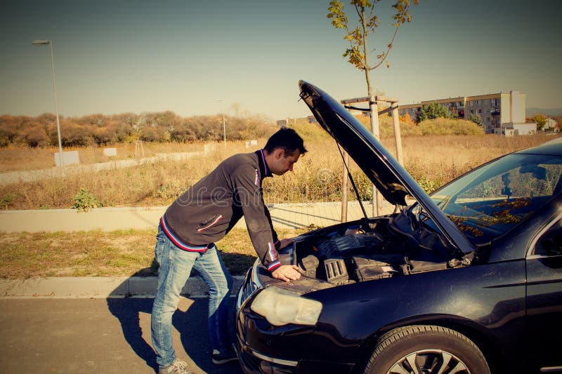 A Young Man is Standing by a Broken Car and Looks Under the Car Hood ...