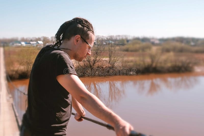 Young Man is Standing on a Suspended Wooden Bridge Over the River ...
