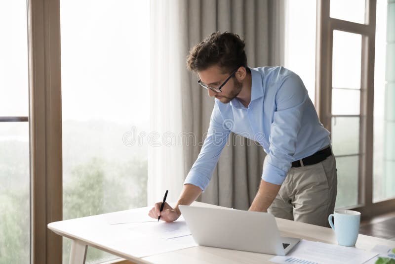 Young Man Standing by Table Review Paper Documents Using Laptop Stock ...