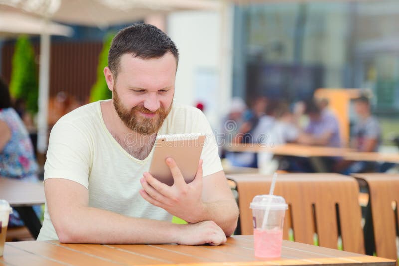 Young Man Student Using a Tablet Computer in a Cafe with a Cool Drink ...