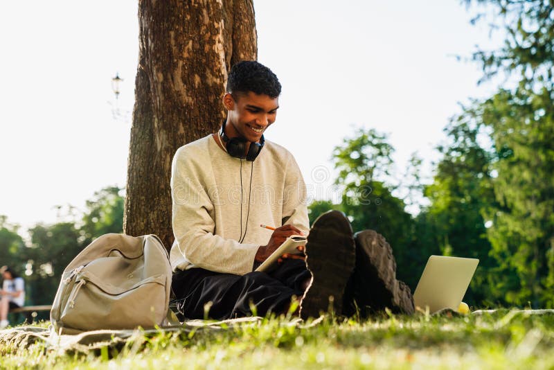 Young Man Studying and Taking Notes while Sitting Under Tree in Park ...