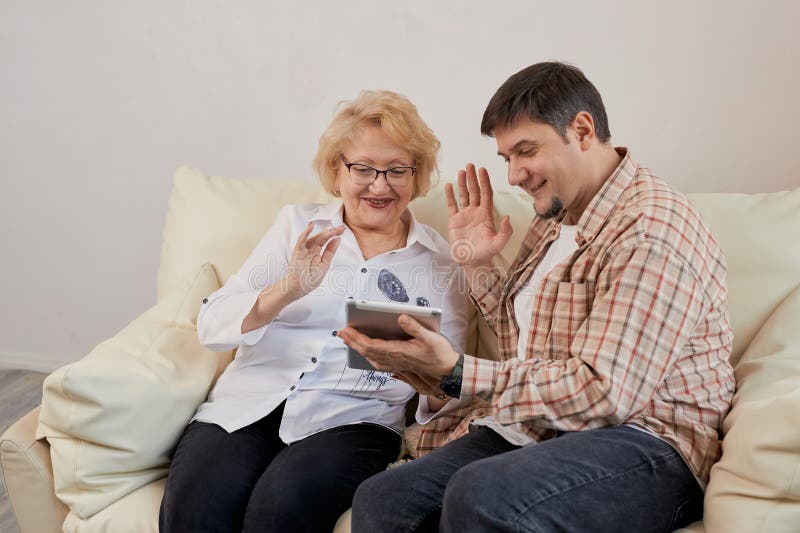 Young Man with Tablet Computer Hugging His Mother on Sofa in Kitchen ...
