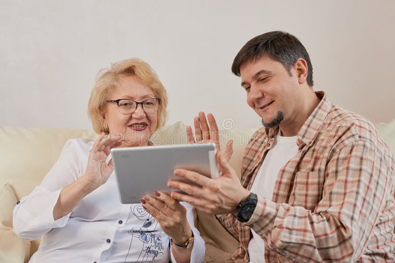 Young Man with Tablet Computer Hugging His Mother on Sofa in Kitchen ...