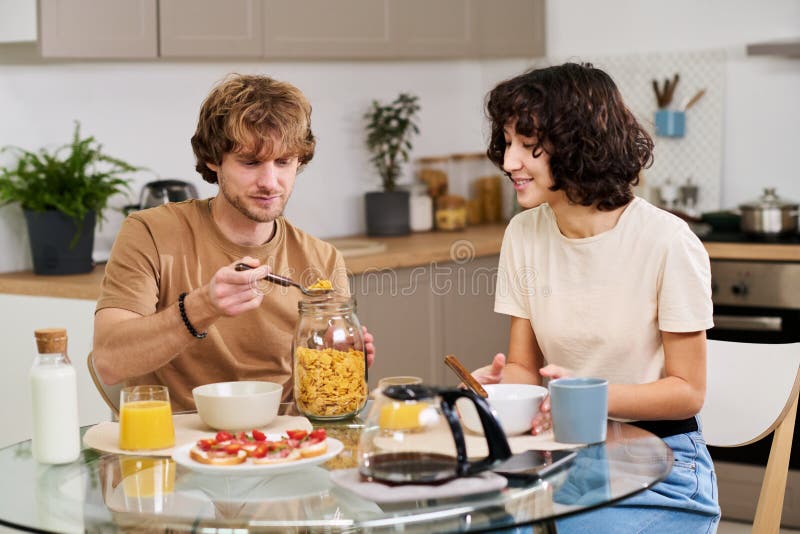 Young Man Taking Some Cornflakes from Jar during Breakfast with His ...
