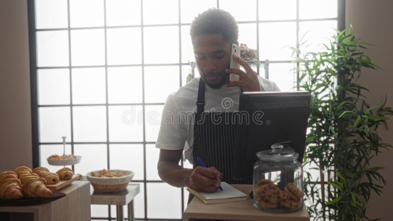 Young Man Talking on Phone and Taking Notes at Counter in Bakery Shop ...