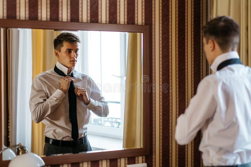 A Young Handsome Man Ties Up a Tie in Front of a Mirror Stock Photo ...