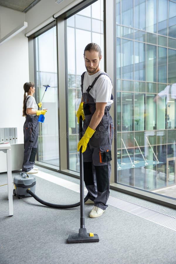 Young Man in Uniform Vacuum Cleaning the Floor in the Conference Room ...