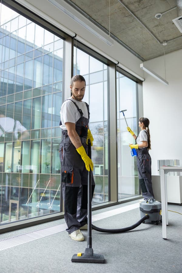 Young Man in Uniform Vacuum Cleaning the Floor in the Conference Room ...