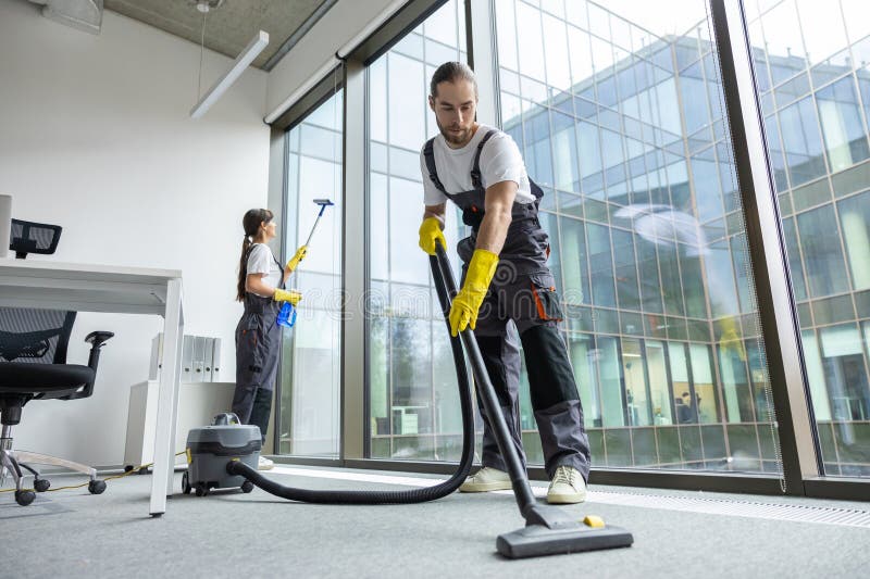 Young Man in Uniform Vacuum Cleaning the Floor in the Conference Room ...
