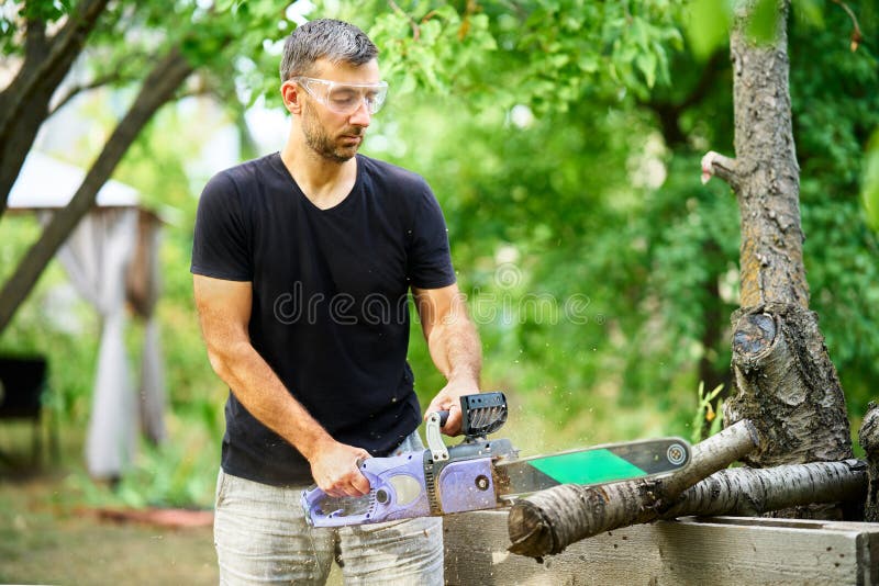 Young Man Using Chainsaw for Cutting Tree Branches at His Backyard ...