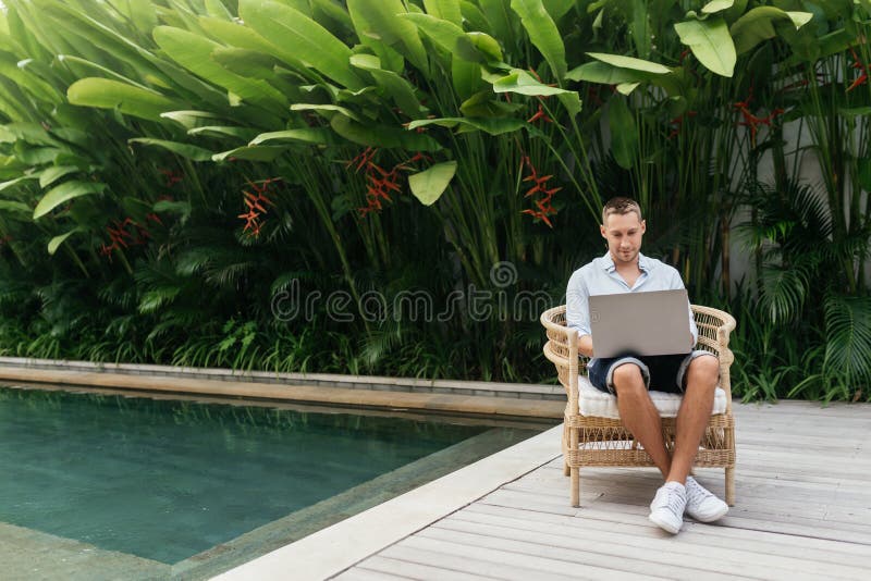 Young Man Using a Laptop Computer in a Garden with a Swimming Pool ...