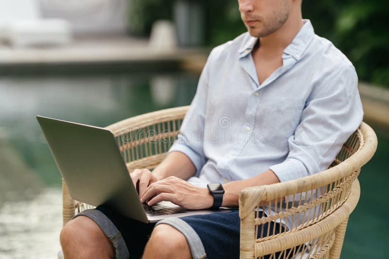 Young Man Using a Laptop Computer in a Garden with a Swimming Pool ...