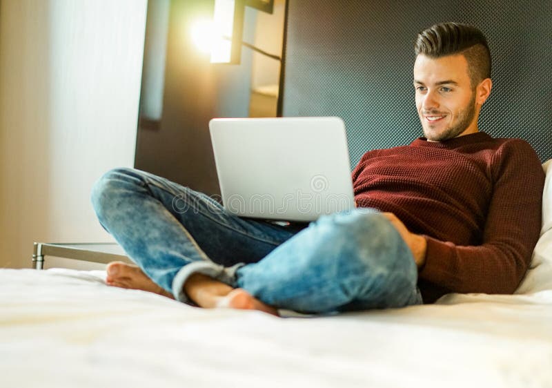 Young Man Using Laptop Computer for Working at Home - Handsome Cheerful Student Relaxing on Bed ...