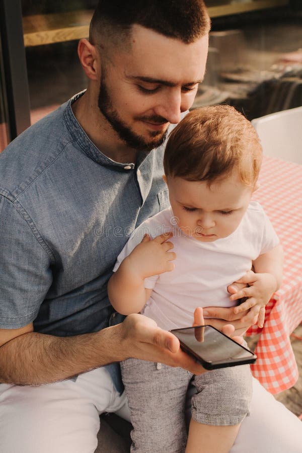 Young Man Using a Phone Mobile for Work and Holding His Son on His Hand ...