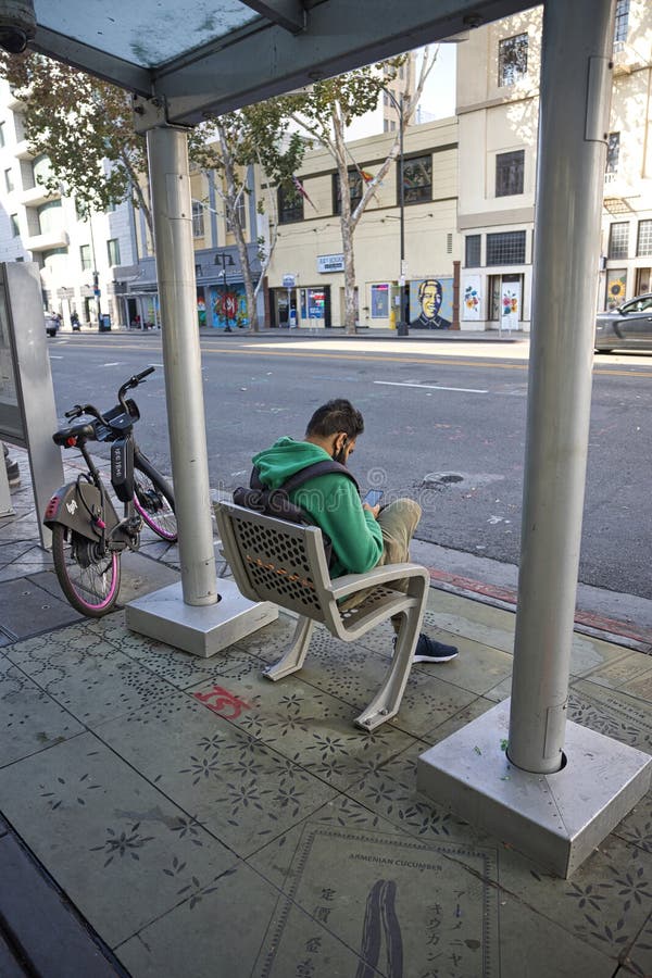 Young Man Using Smartphone Waiting For Bus At Bus Stop Editorial Stock