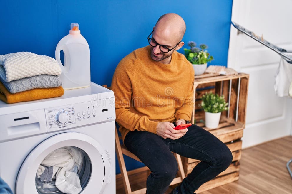 Young Man Using Smartphone Waiting for Washing Machine at Laundry Room ...