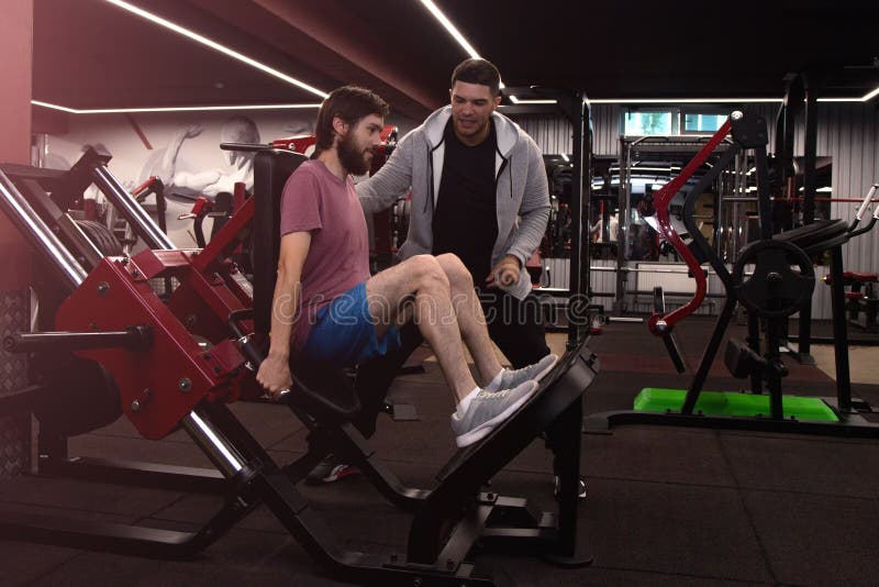 Young Man Using Weights Press Machine for Legs with Assistance of Her ...