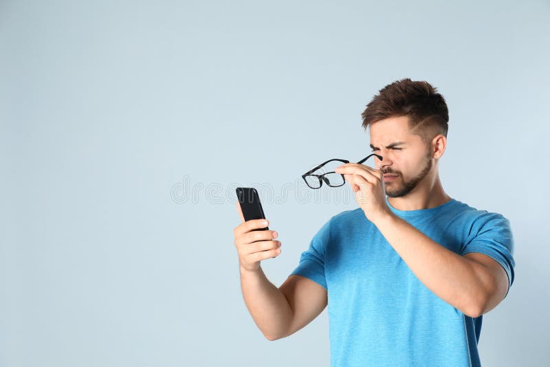 Young Man With Vision Problems Using Smartphone On Grey Background ...