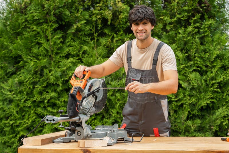 Young Man in a Work Uniform Repairs a Miter Saw Using a Screwdriver ...
