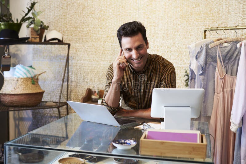 Young Man Working at Clothes Shop on Phone, Using Computer Stock Image ...