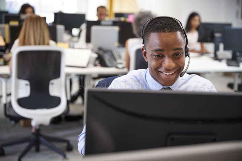 Young Man Working at Computer with Headset in Busy Office Stock Photo ...