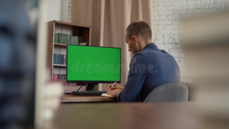 Man Working at Desk Using Computer with Green Mock-up Screen in Cozy ...