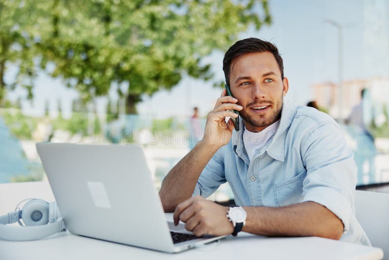 Young Man Working Outdoors with a Laptop, Engaged in a Phone Call ...