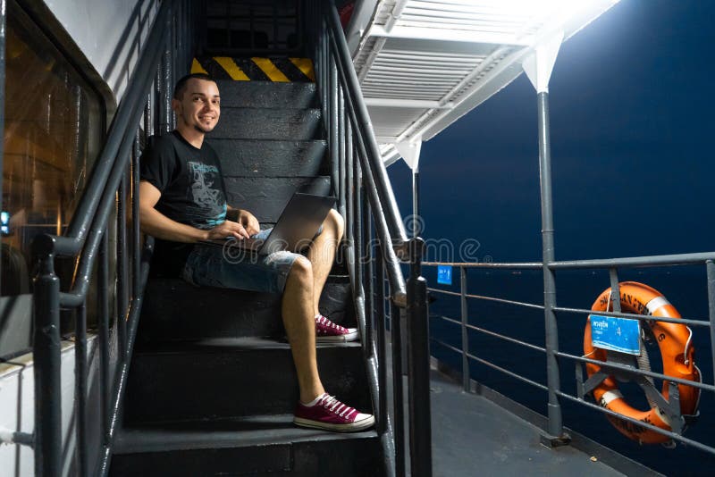 A Young Man Works on a Laptop on the Deck of a Ship. Remote Work Stock ...