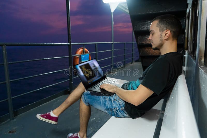 A Young Man Works on a Laptop on the Deck of a Ship. Remote Work ...