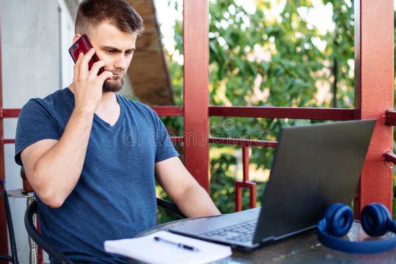 A Bearded Young Man is Using Computer Laptop and Smartphone for Working ...