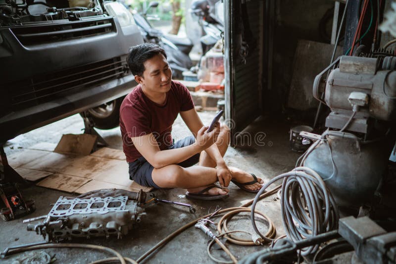 Young Mechanic Using a Cell Phone while Sitting on the Floor Resting ...