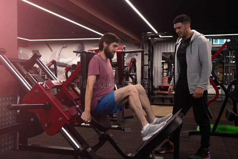 Young Man Using Weights Press Machine for Legs with Assistance of Her ...