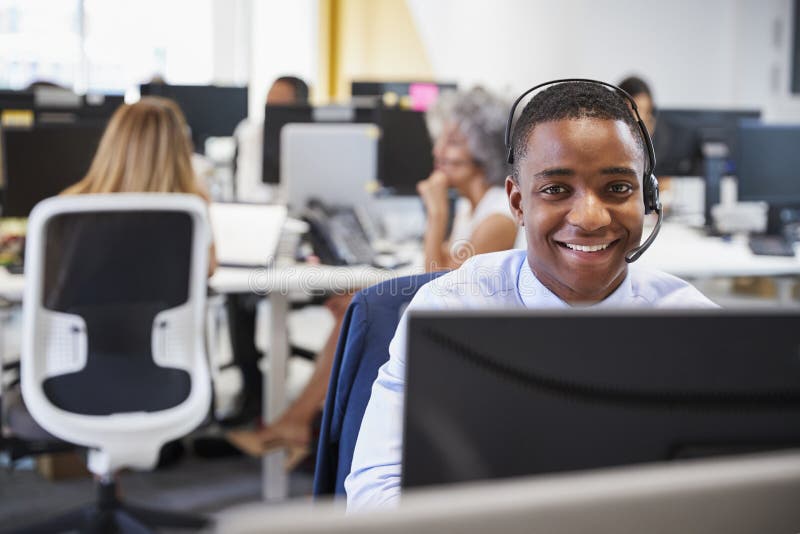 Young Man Working at Computer with Headset in Busy Office Stock Photo ...
