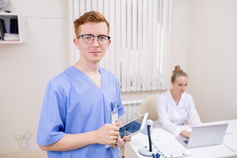 Young Mobile Intern in Eyeglasses and Blue Medical Uniform Using ...