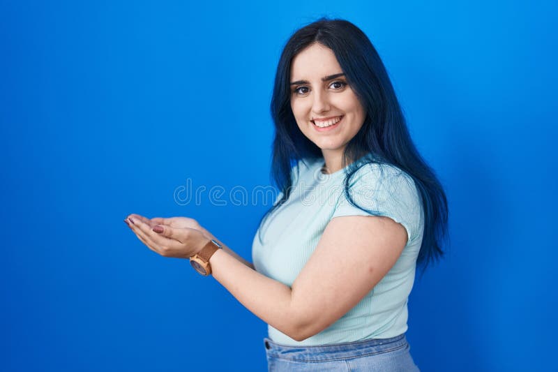 Young Modern Girl With Blue Hair Standing Over Blue Background Pointing
