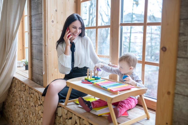 Young Mom Playing Game with Daughter on Windowsill, Talking on Phone ...