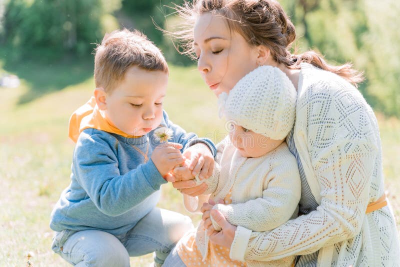 A Young Mother Sits On The Grass With Her Three Year Old Son And One
