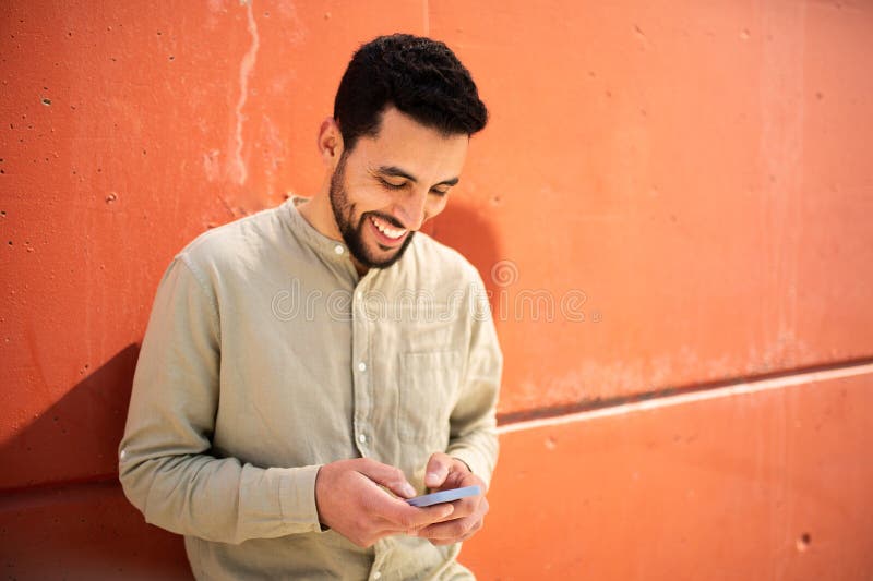 Young North African Man Using Mobile Phone Against Orange Wall Stock ...