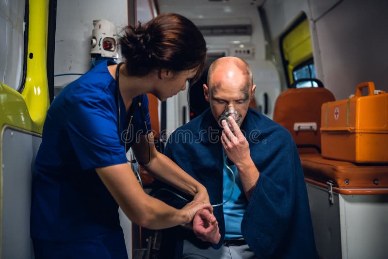 Young Nurse In Uniform Holds A Hand Of Man Who Sits In Oxygen Mask In